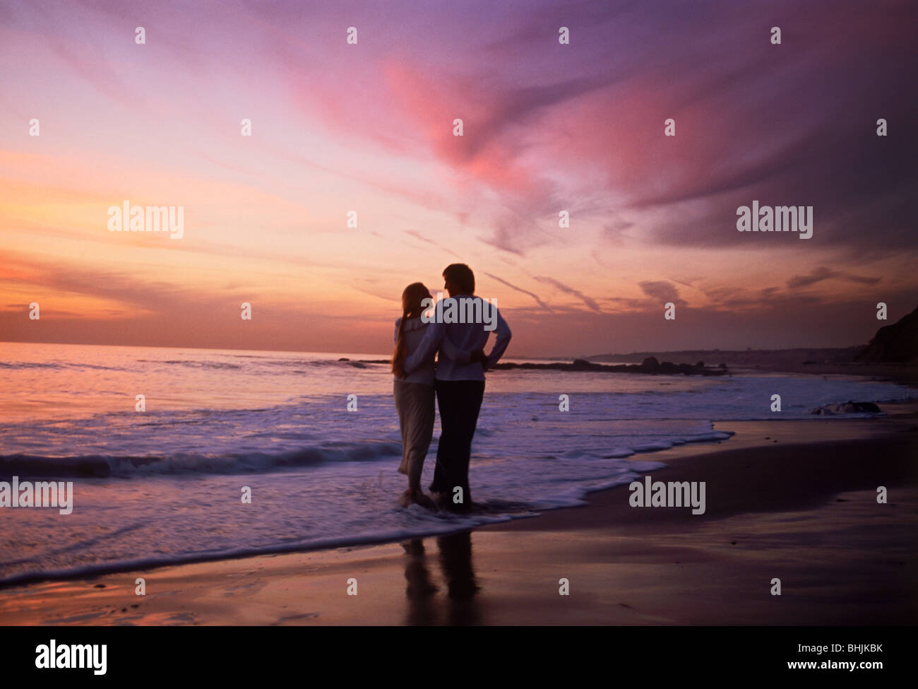 Couple walking through shore surf at sunset near Laguna Beach ...