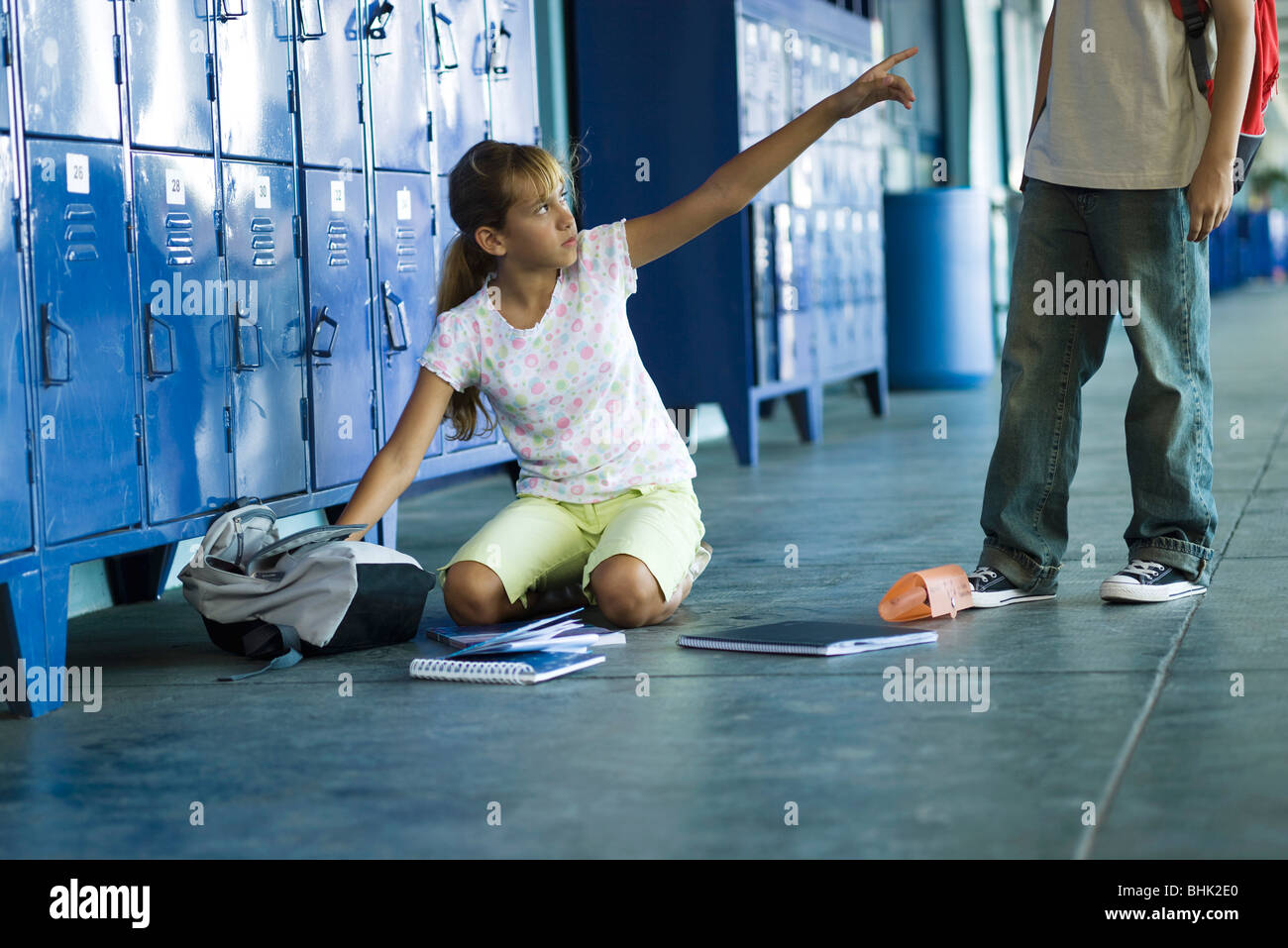 Female junior high student sitting on floor pointing angrily up at boy ...