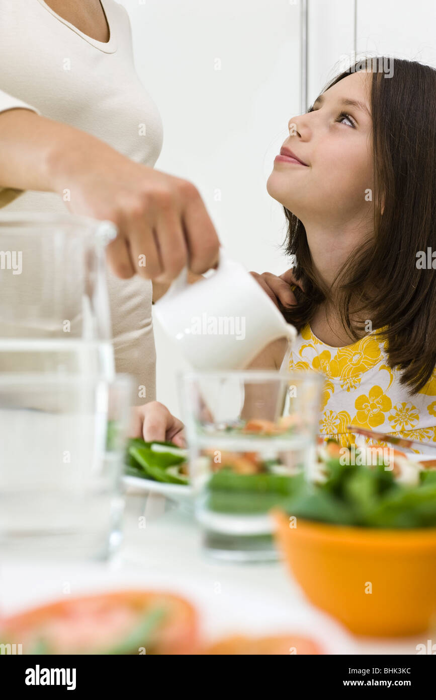 Girl sitting at table looking up at mother serving food Stock Photo - Alamy