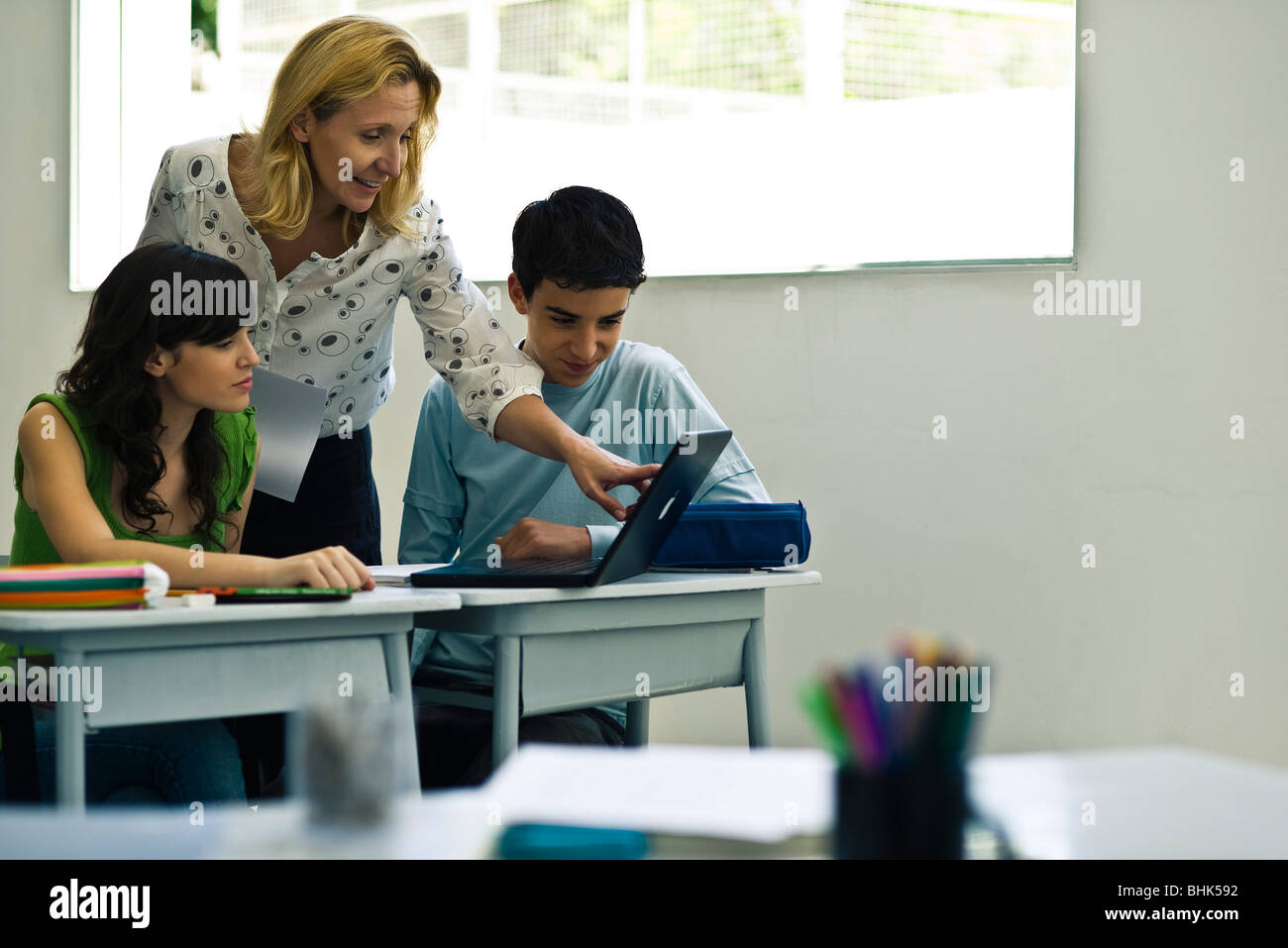 Teacher helping students using laptop computer in class Stock Photo - Alamy