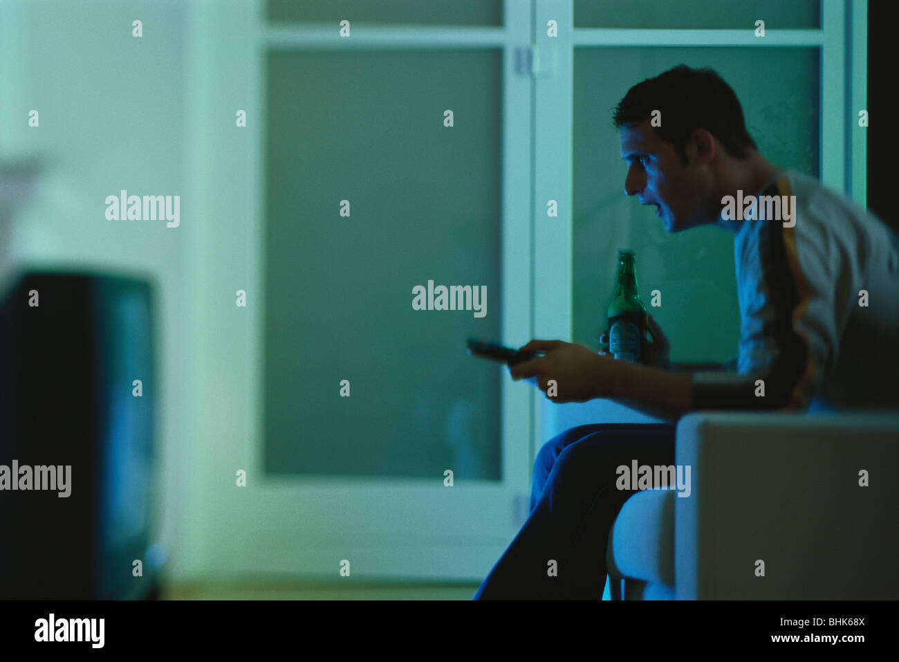 Man watching TV, holding beer and remote, side view Stock Photo - Alamy