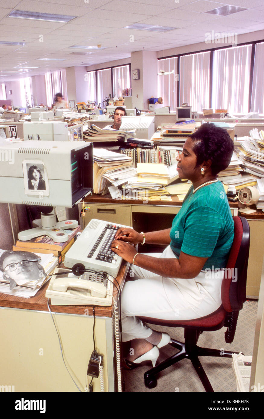black woman works on computer system at office desk at local newspaper ...