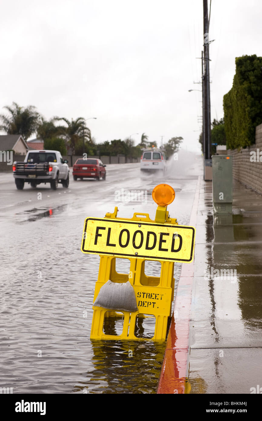 A car kicks up a pool of rainwater over a street flooded sign during ...