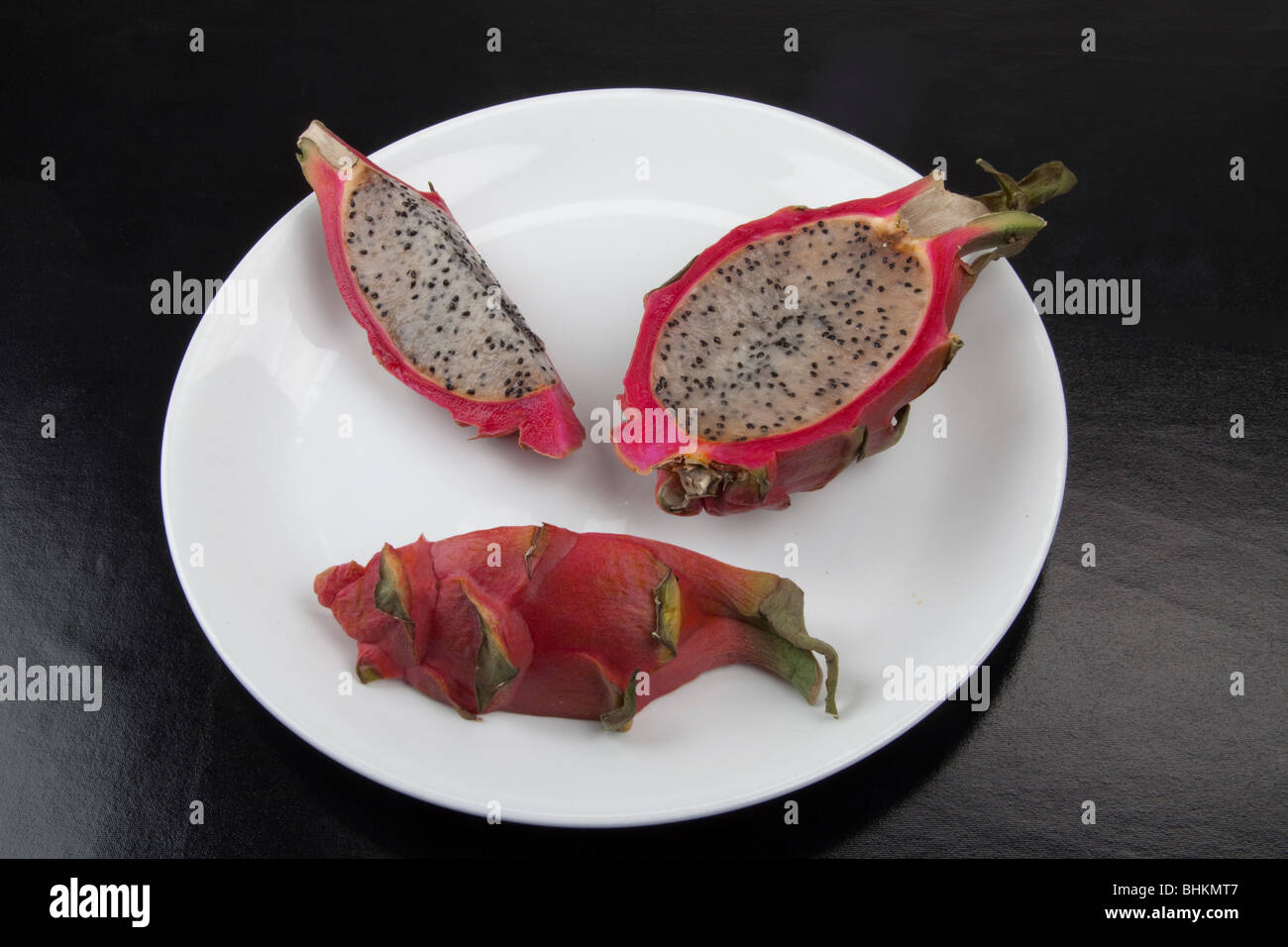 deep red Dragon fruit (pitaya) split in quarters on white plate, black ...