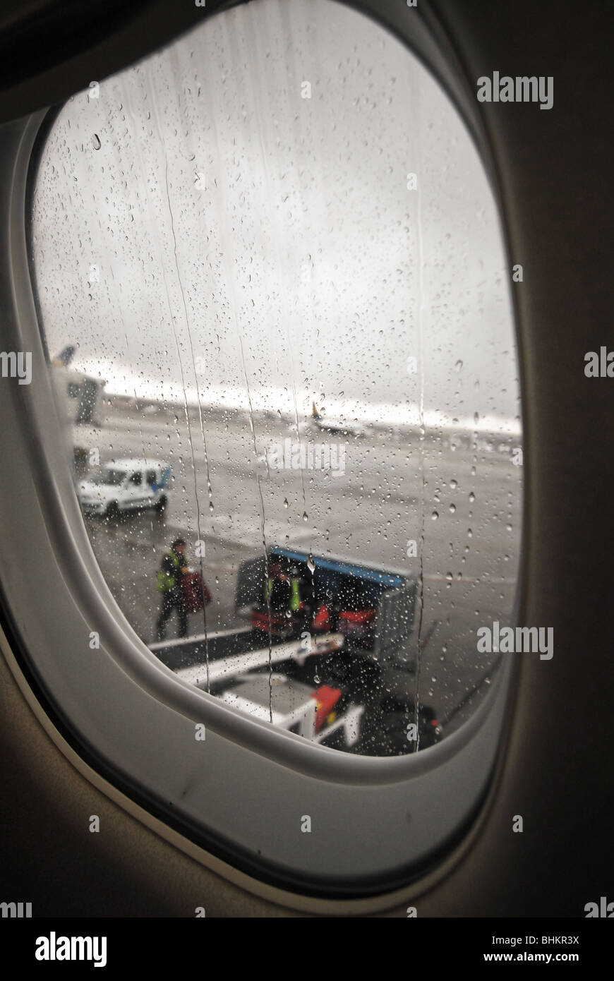 Baggage handlers load luggage onto a passenger plane in the rain Stock ...