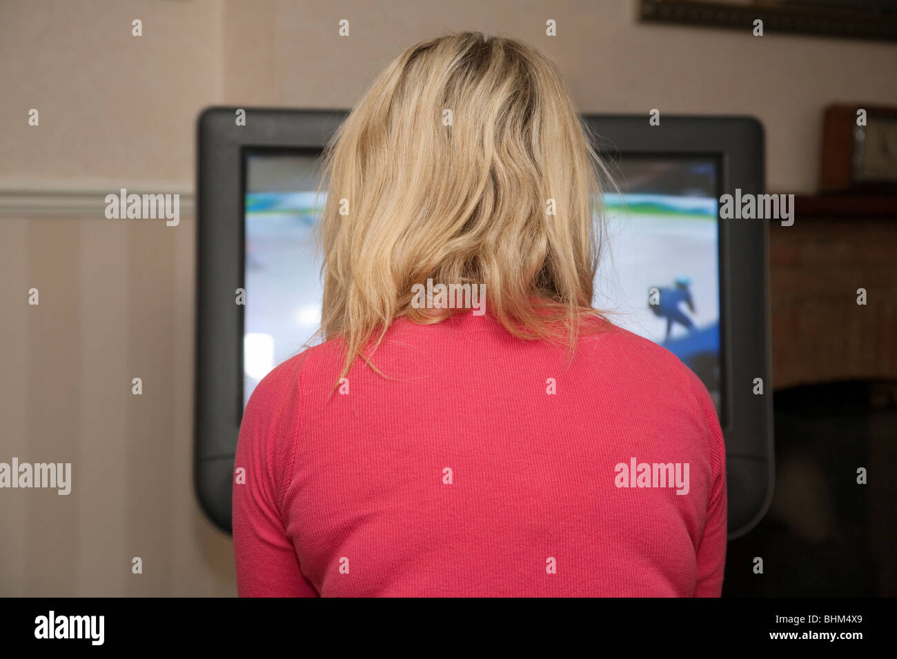Rear view of a blonde teenage girl watching TV sitting in front of the ...