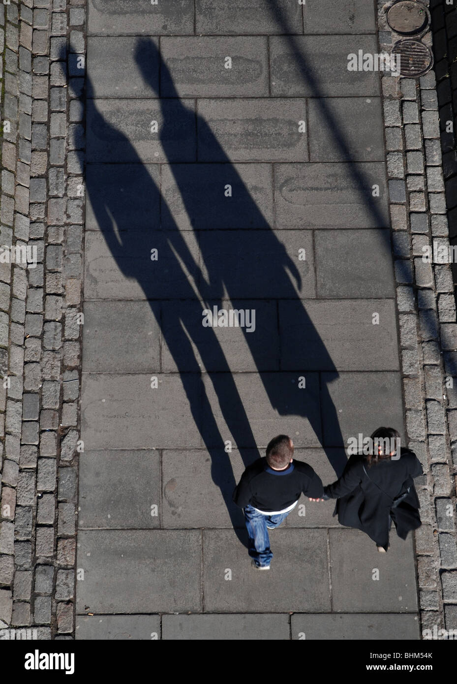 A couple holding hands and casting a long shadow Stock Photo - Alamy