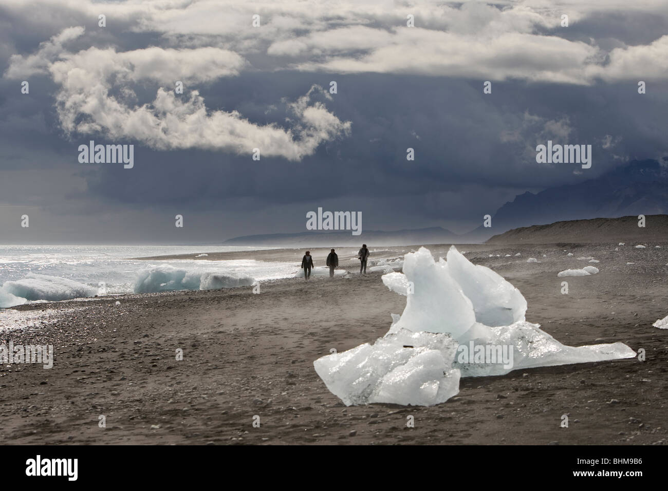 Tourists walking between melting ice cubes at the beach below ...