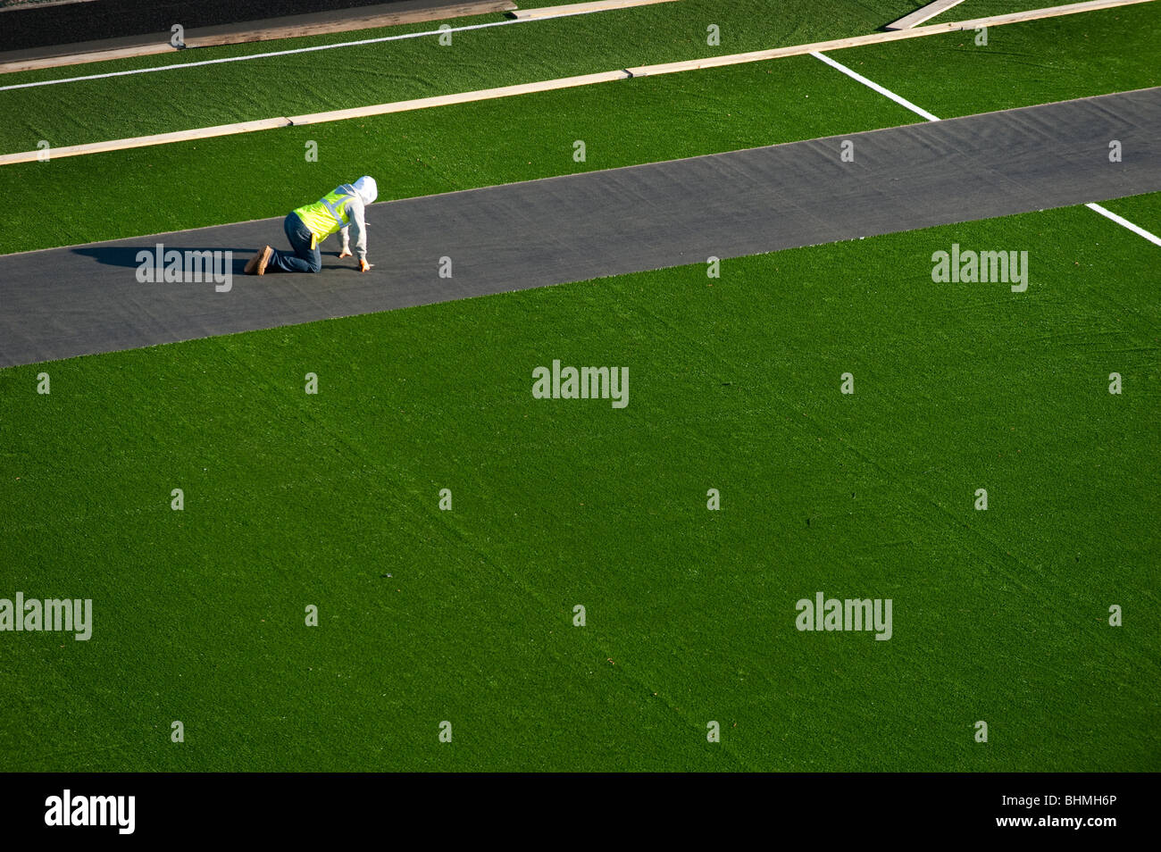 image of worker laying green astroturf surface on sports playing field ...