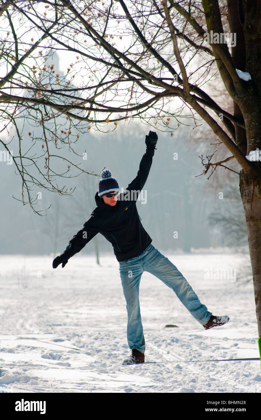 Guy practices balance on a rope, in a snow covered English Garden with ...