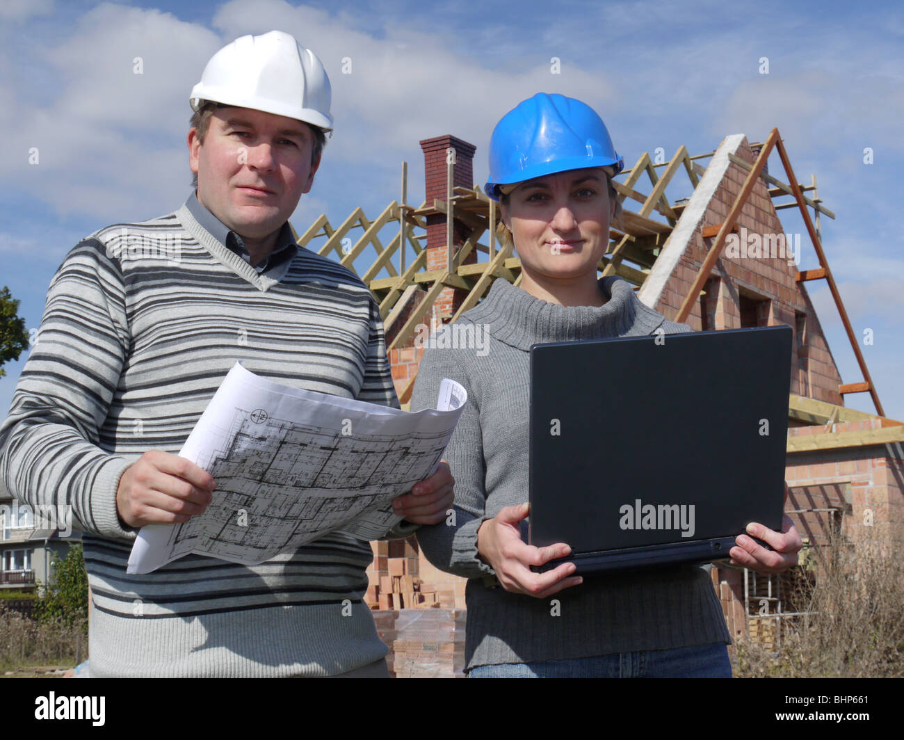 Female and male building engineers standing against unfinished brick ...