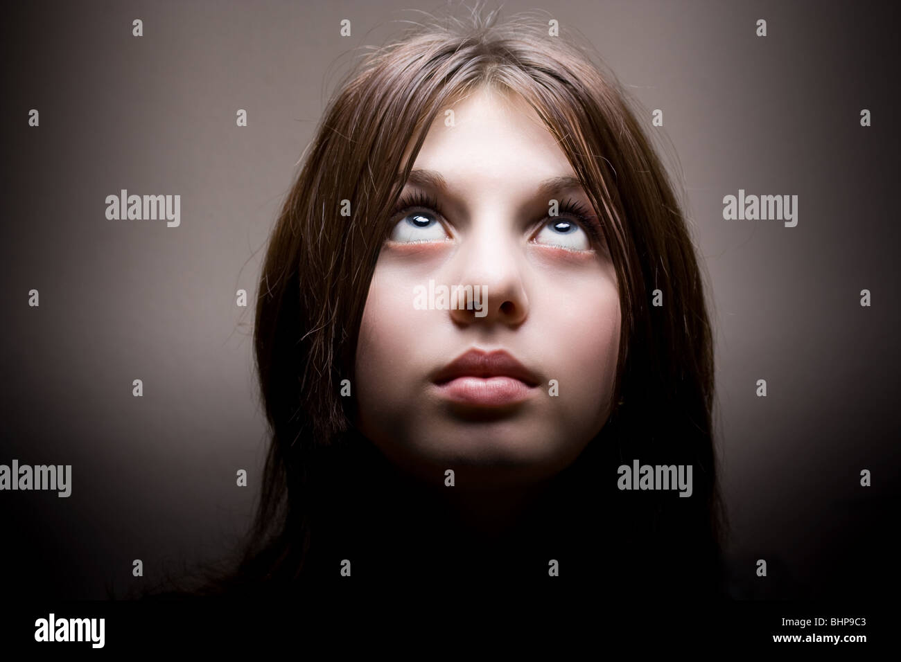 Striking image of a beautiful young woman looking up with light above ...