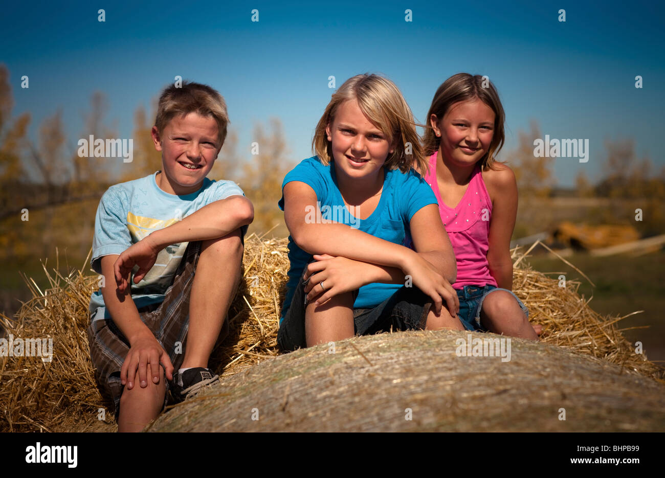 3 Farm Kids Seated On Bales; Redvers, Saskatchewan, Canada Stock Photo ...