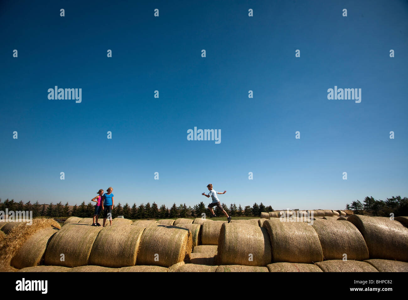 Two Girls Watch Boy Jump Over Space Between Bales; Redvers ...