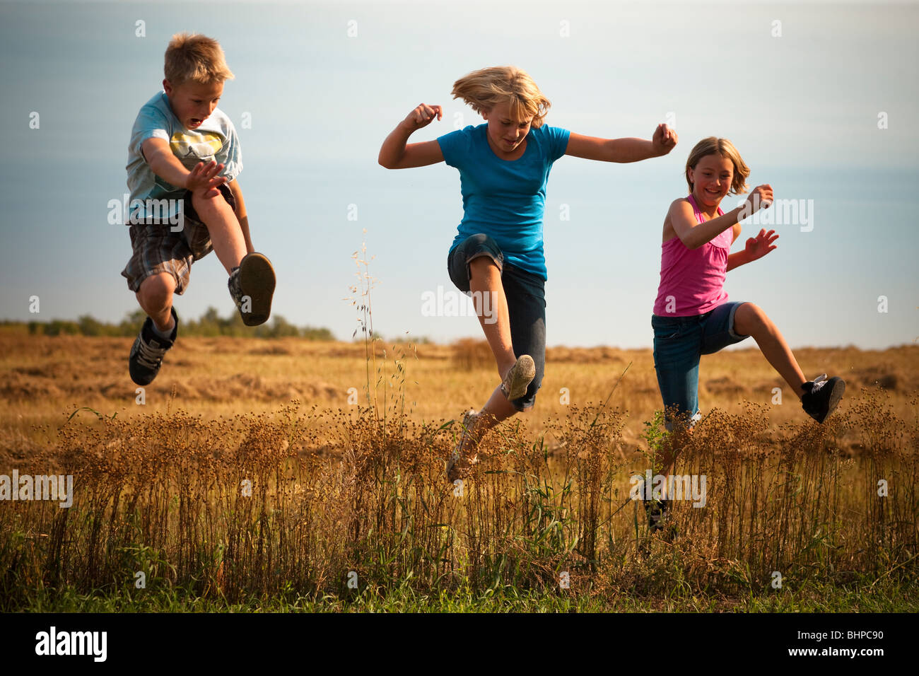 Three Tween Kids Jumping The Swath In Flax Field; Redvers, Saskatchewan ...