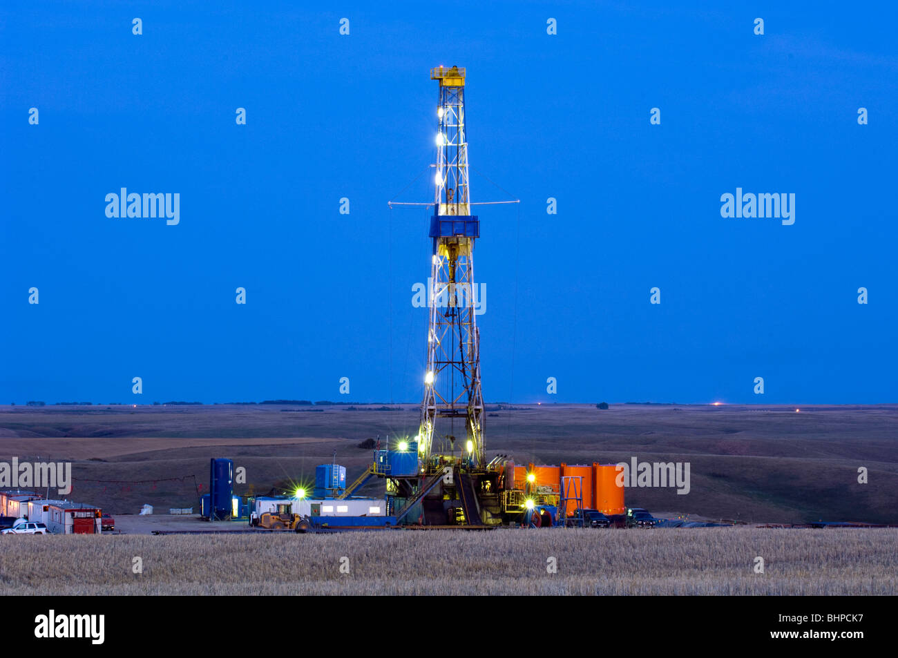 Oil drilling rig in evening light with lights on sitting in a wheat ...