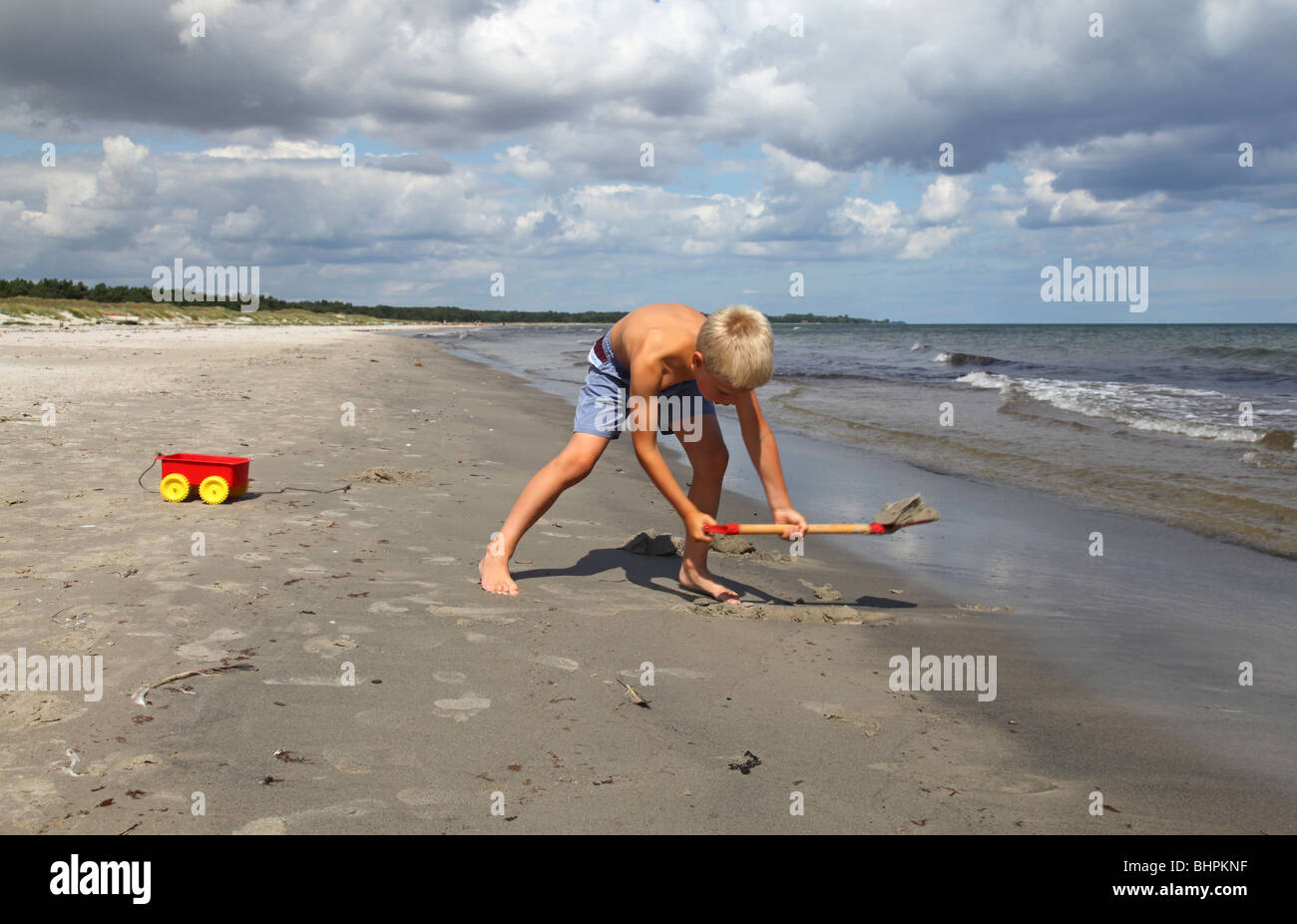 Young blonde boy digging in the sand on beach Stock Photo - Alamy