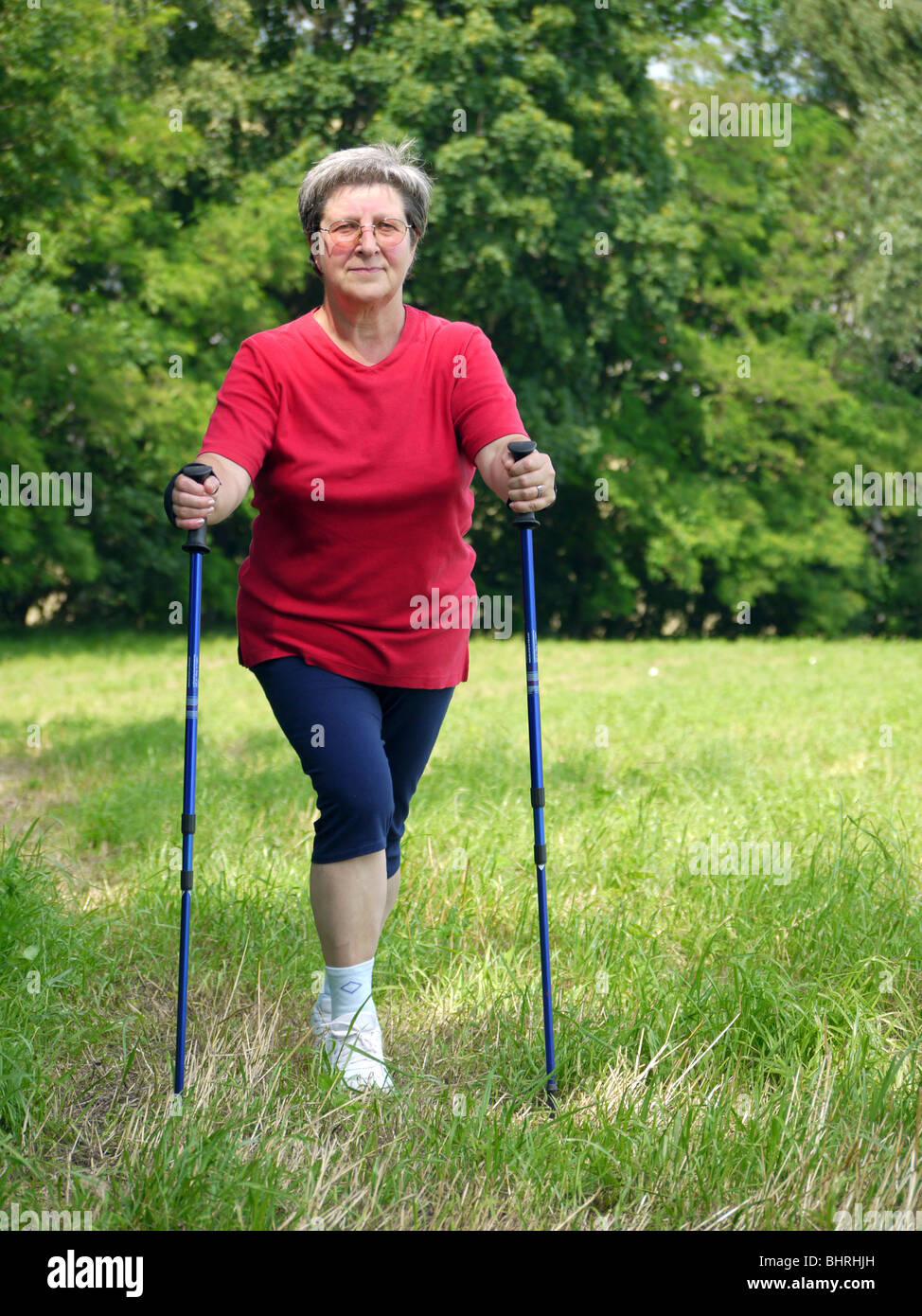 Senior woman doing a series of warm-up exercises with walking poles ...