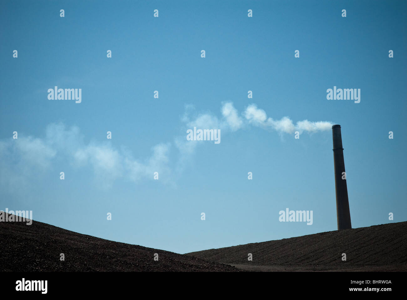 Smoke stack spewing emissions with mining slag in foreground creating ...