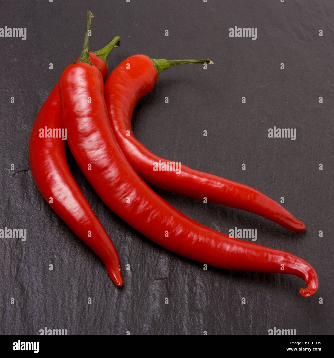 Three vibrant red chillis on a backdrop of dark slate Stock Photo - Alamy