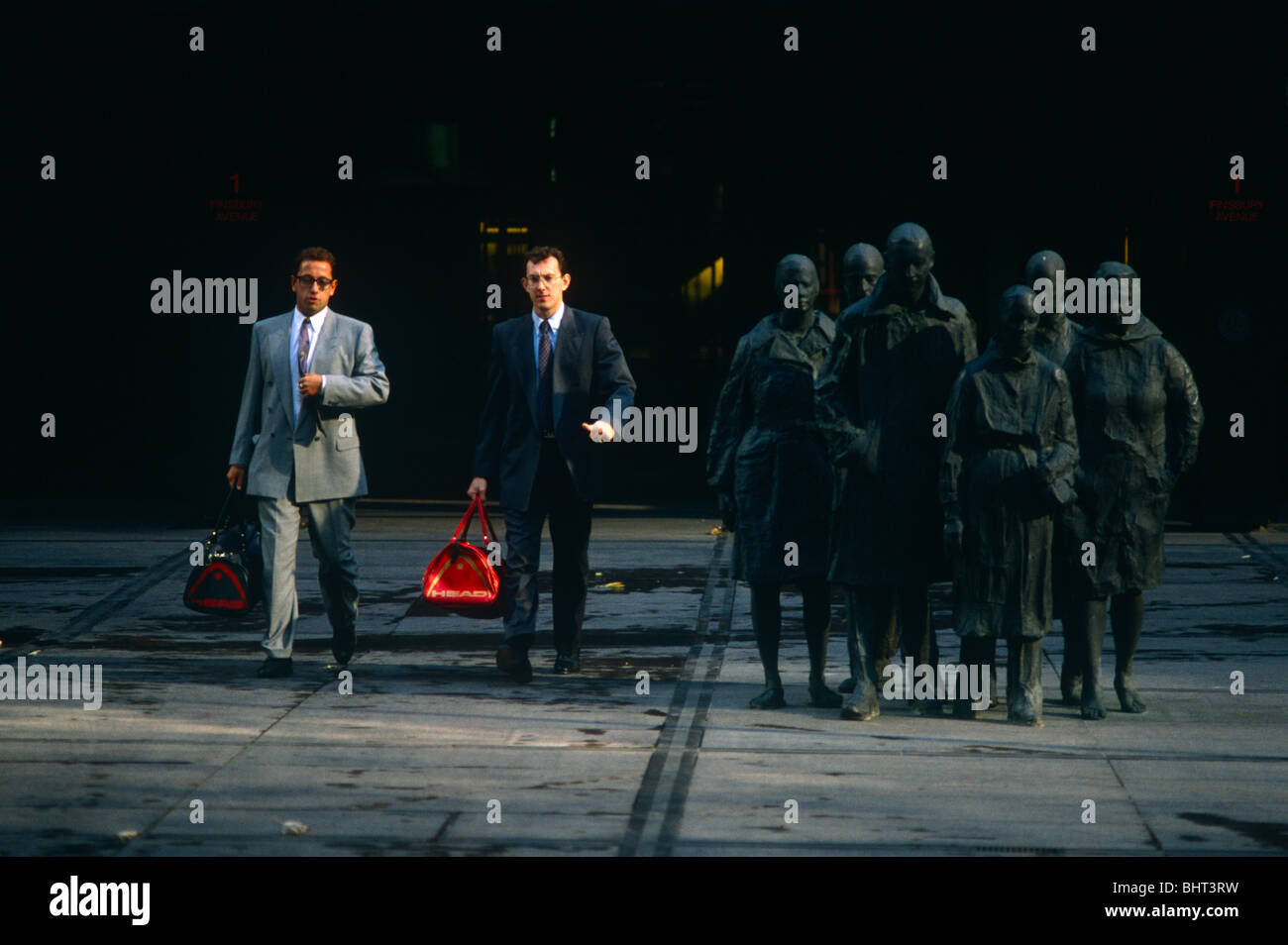 Two city office workers walk briskly past a series of statues of ...
