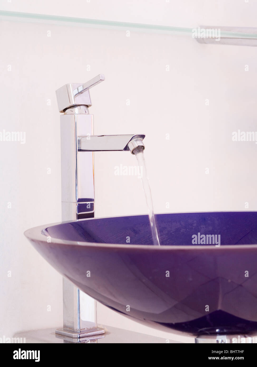 Close-up of angular chrome tap pouring water into circular black glass ...