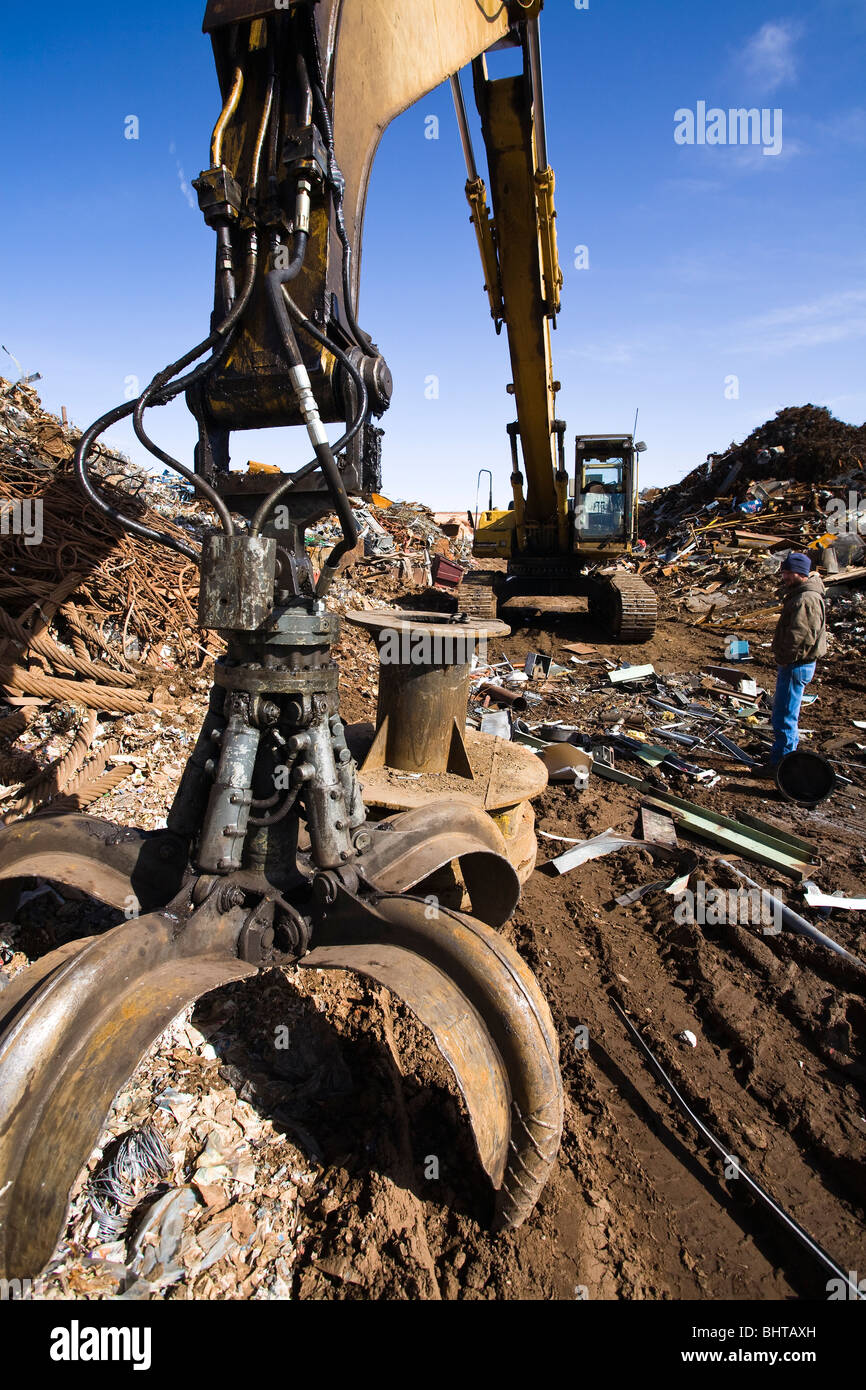 Excavating machine, with large grapple claw, at scrap metal yard. Man ...