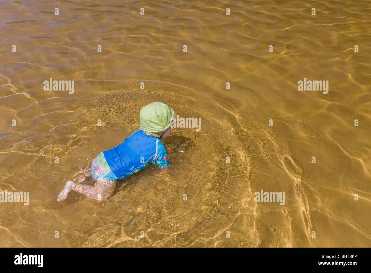 Baby swimming or crawling in shallow water with sand base at river ...