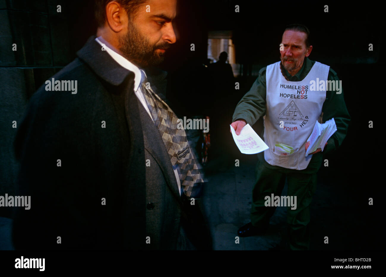 A homeless charity worker (chugger) hands out leaflets to an uncaring ...