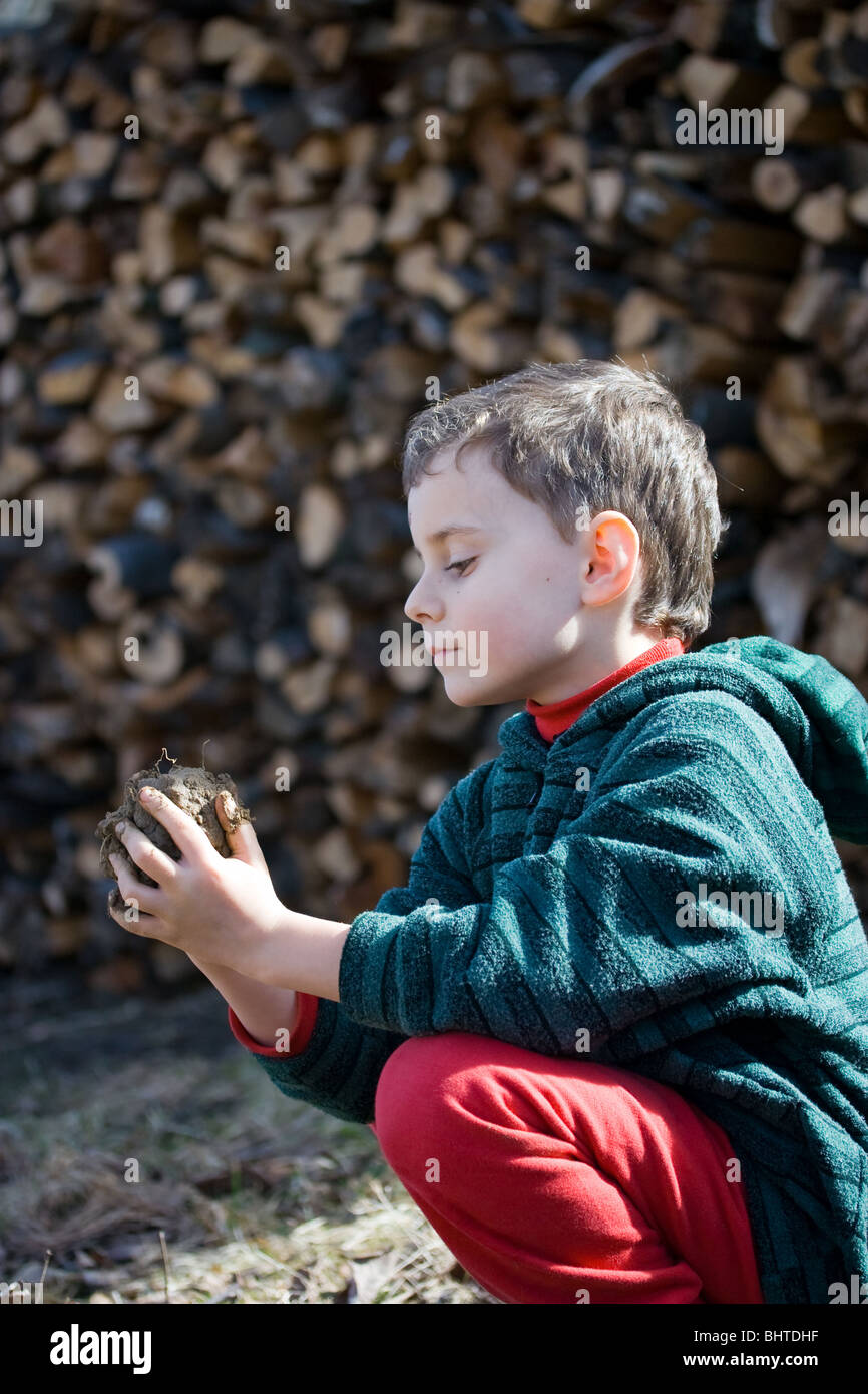 Child modeling with mud with a stack of logs in the background Stock ...