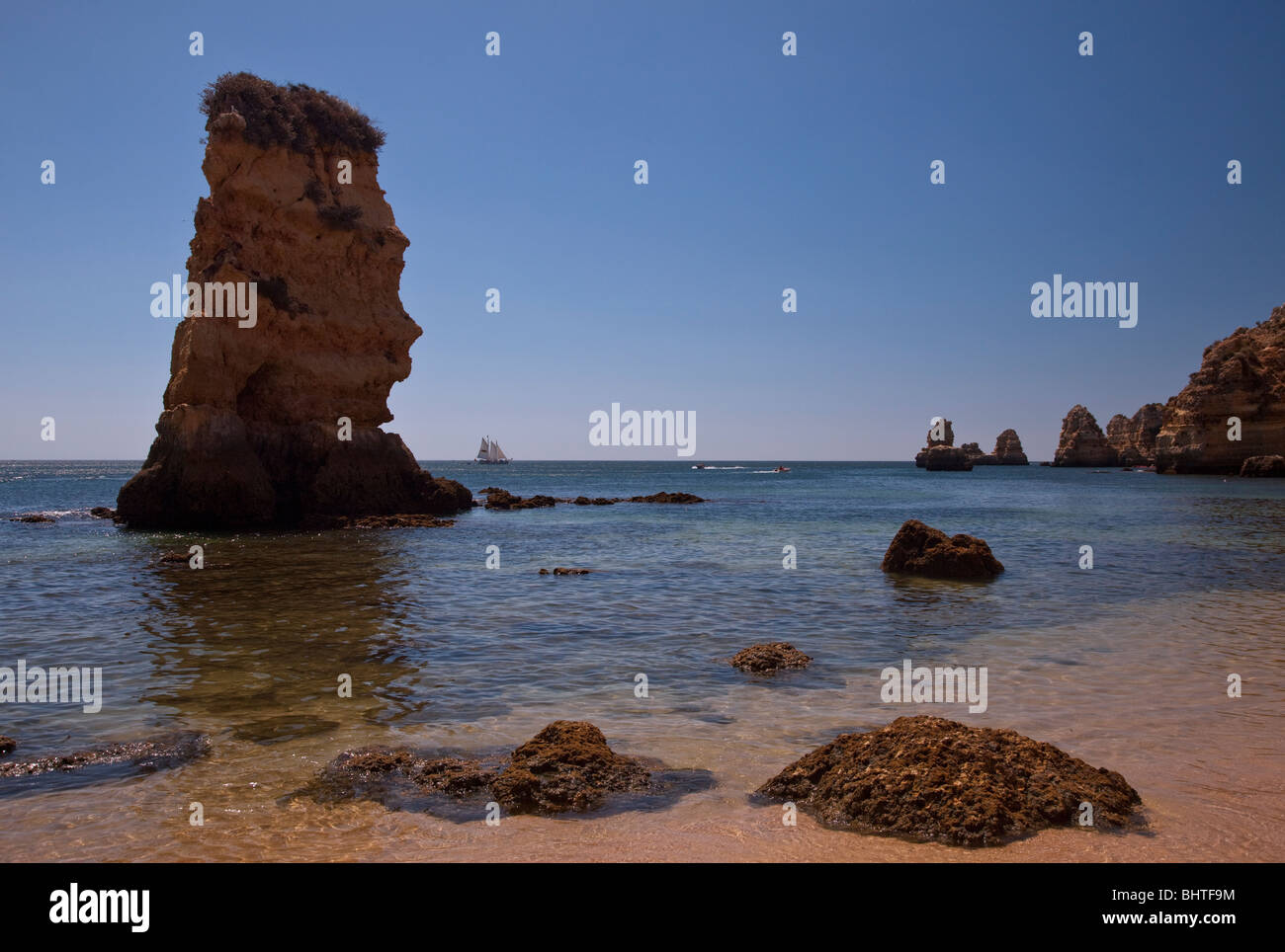 Rocks in the sea and the beach under a blue sky in Algarve with a boat ...