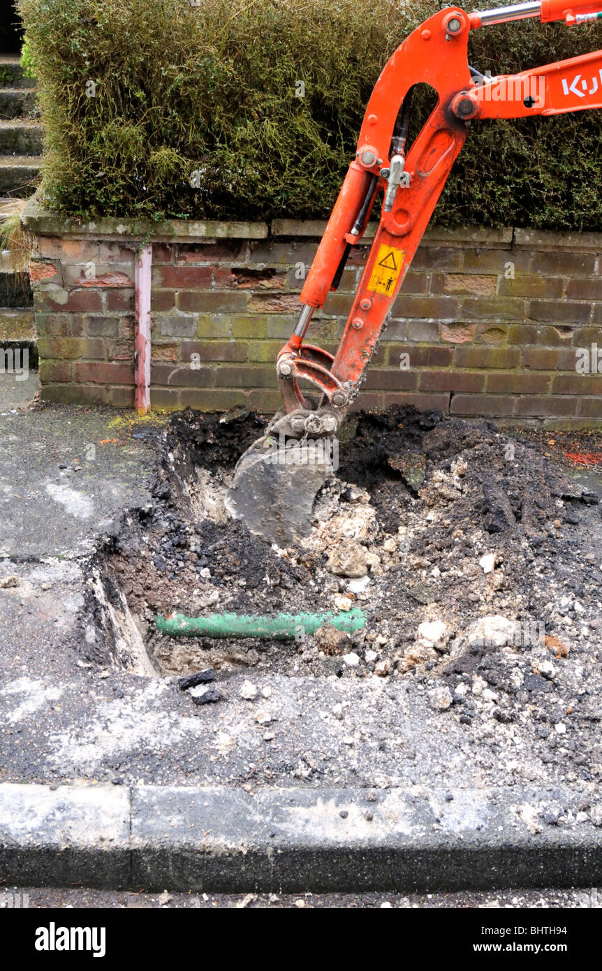 Mini digger digging up the pavement to replace gas pipe Stock Photo - Alamy