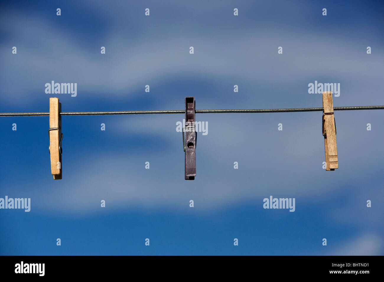 three clothes pegs hanging on a washing line against a bright blue sky ...