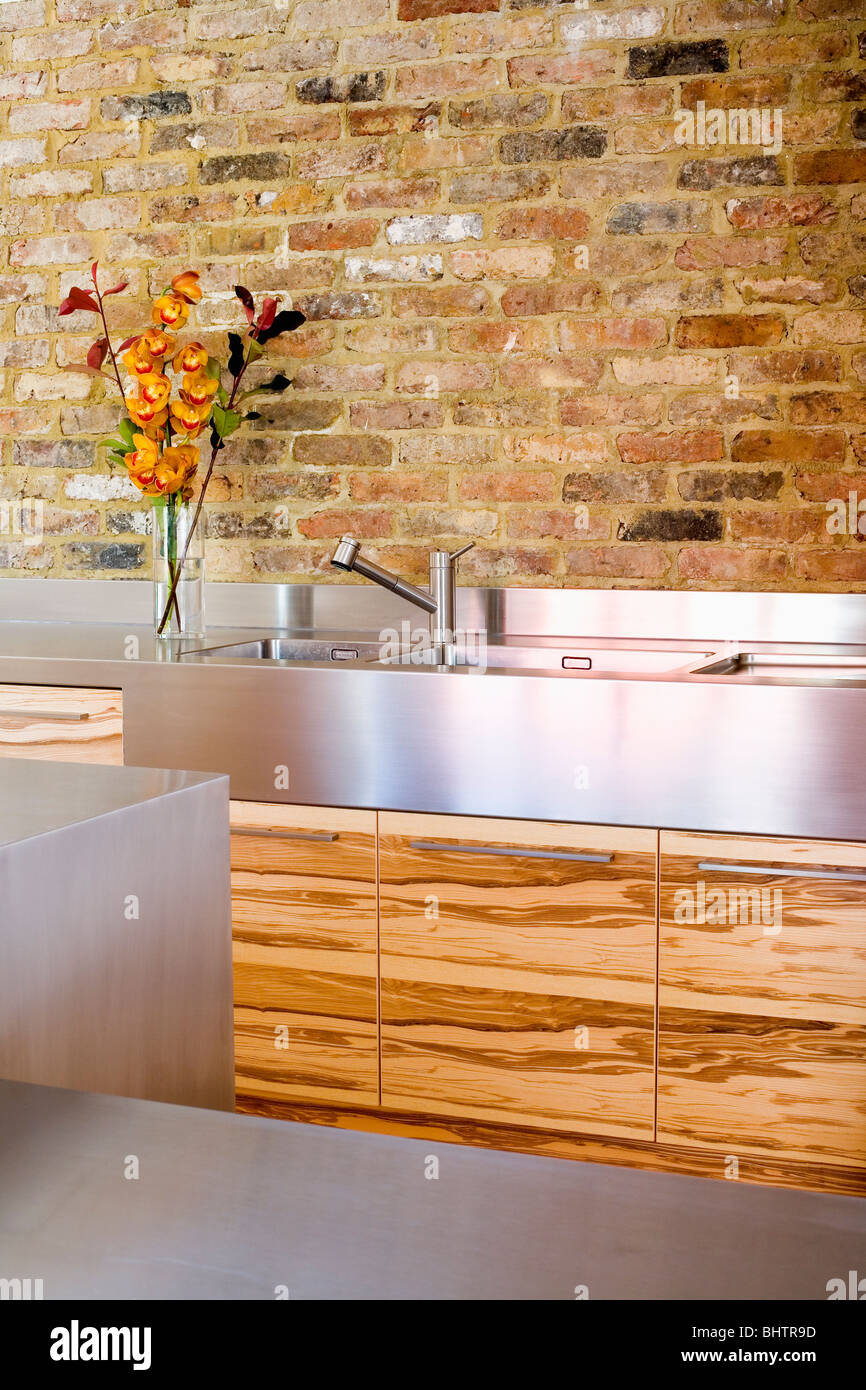 Sink in fitted unit with stainless steel top below exposed brick wall ...
