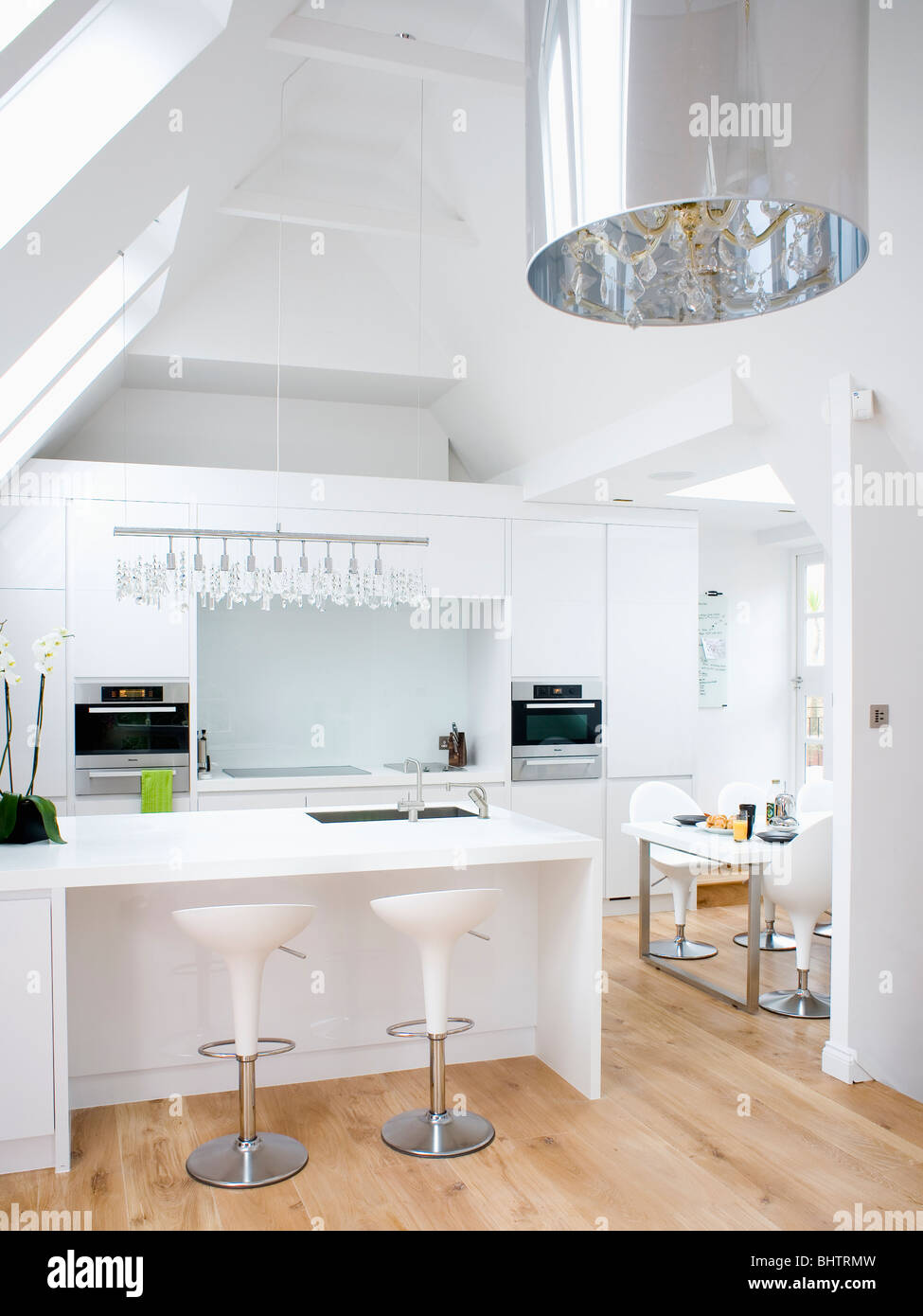 White "Bombo" stools at breakfast bar in modern white loft conversion kitchen with wooden ...