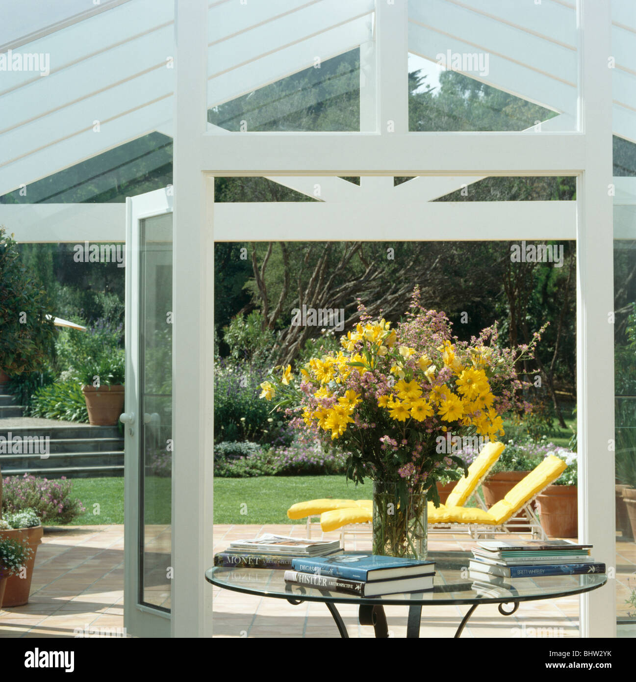 Vase of yellow flowers on circular glass table in front of open glass ...