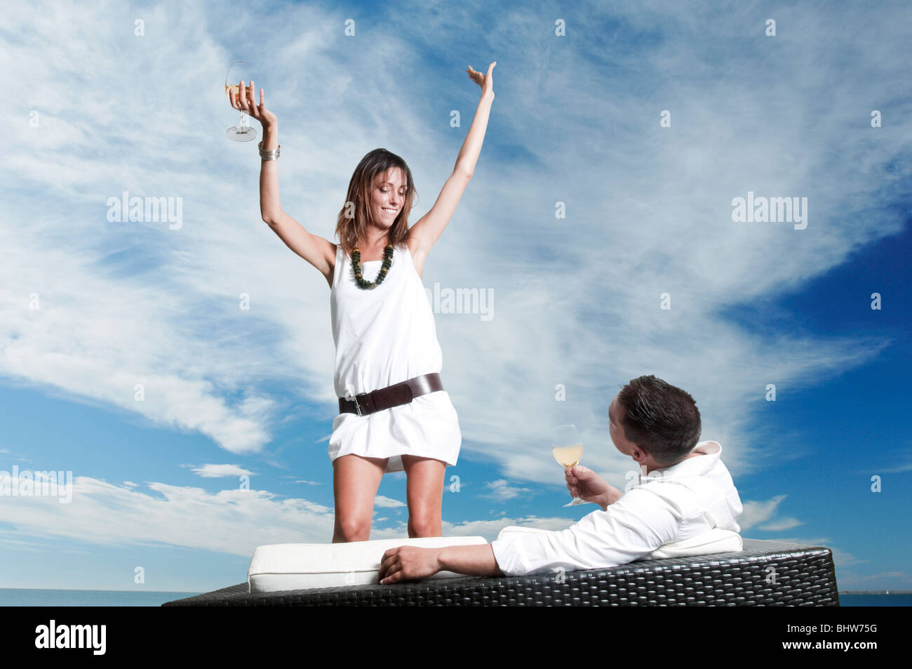 Young woman with white wine dancing next to couch with young man and ...
