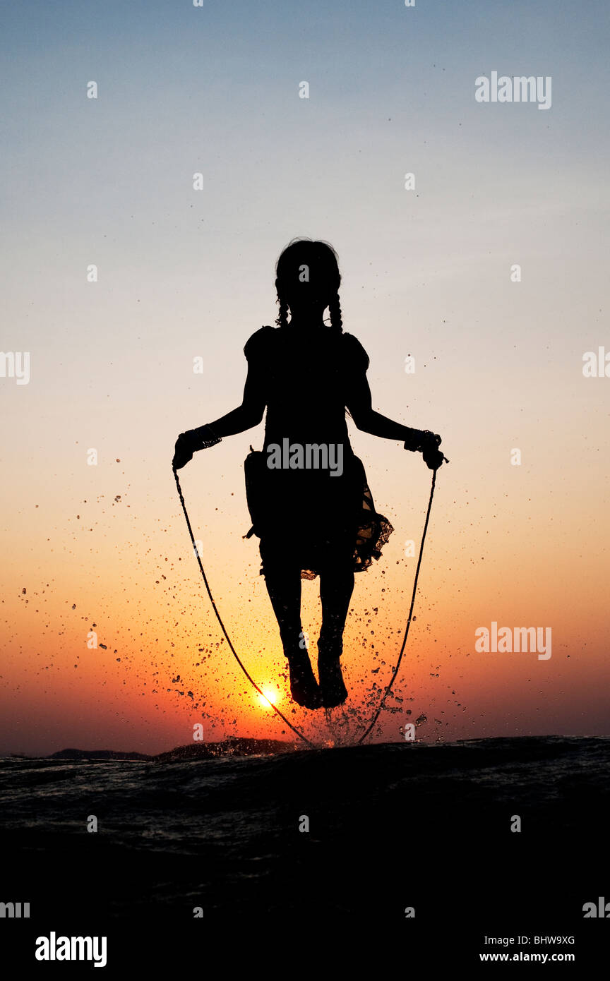 Silhouette of a young Indian girl skipping in water at sunset. India ...
