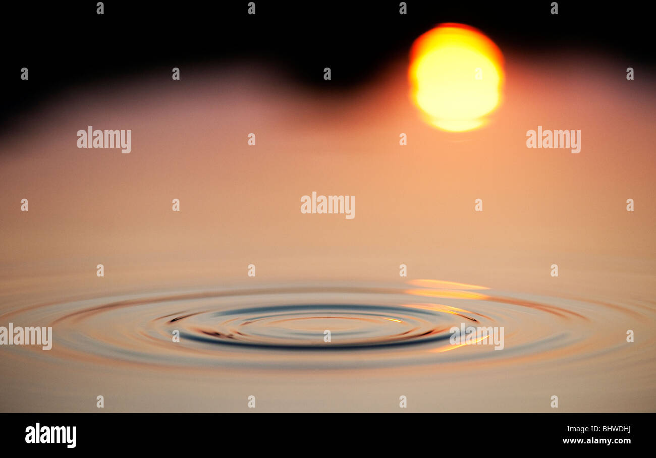 Water drops and ripples in a pool with reflected sunrise background ...