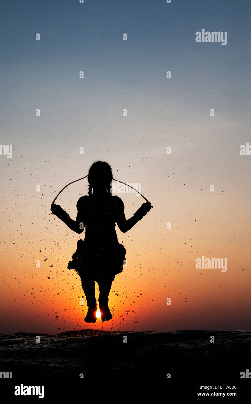 Silhouette of a young Indian girl skipping in water at sunset. India ...