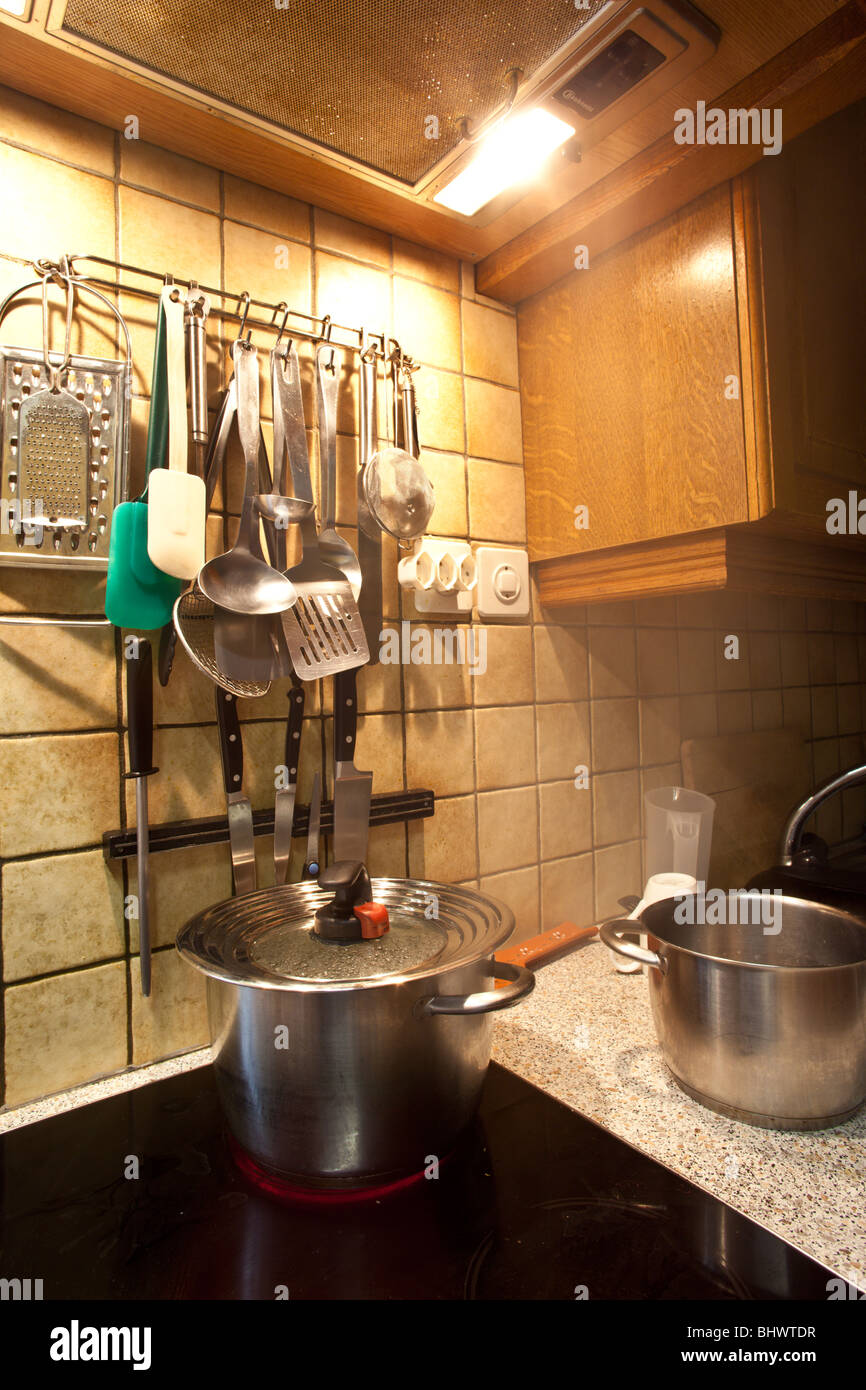 A pot of boiling water sits on a ceramic burner, clutter of kitchen ...