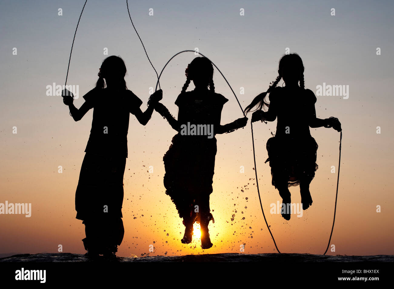Silhouette of young Indian girls skipping in water at sunset. India ...