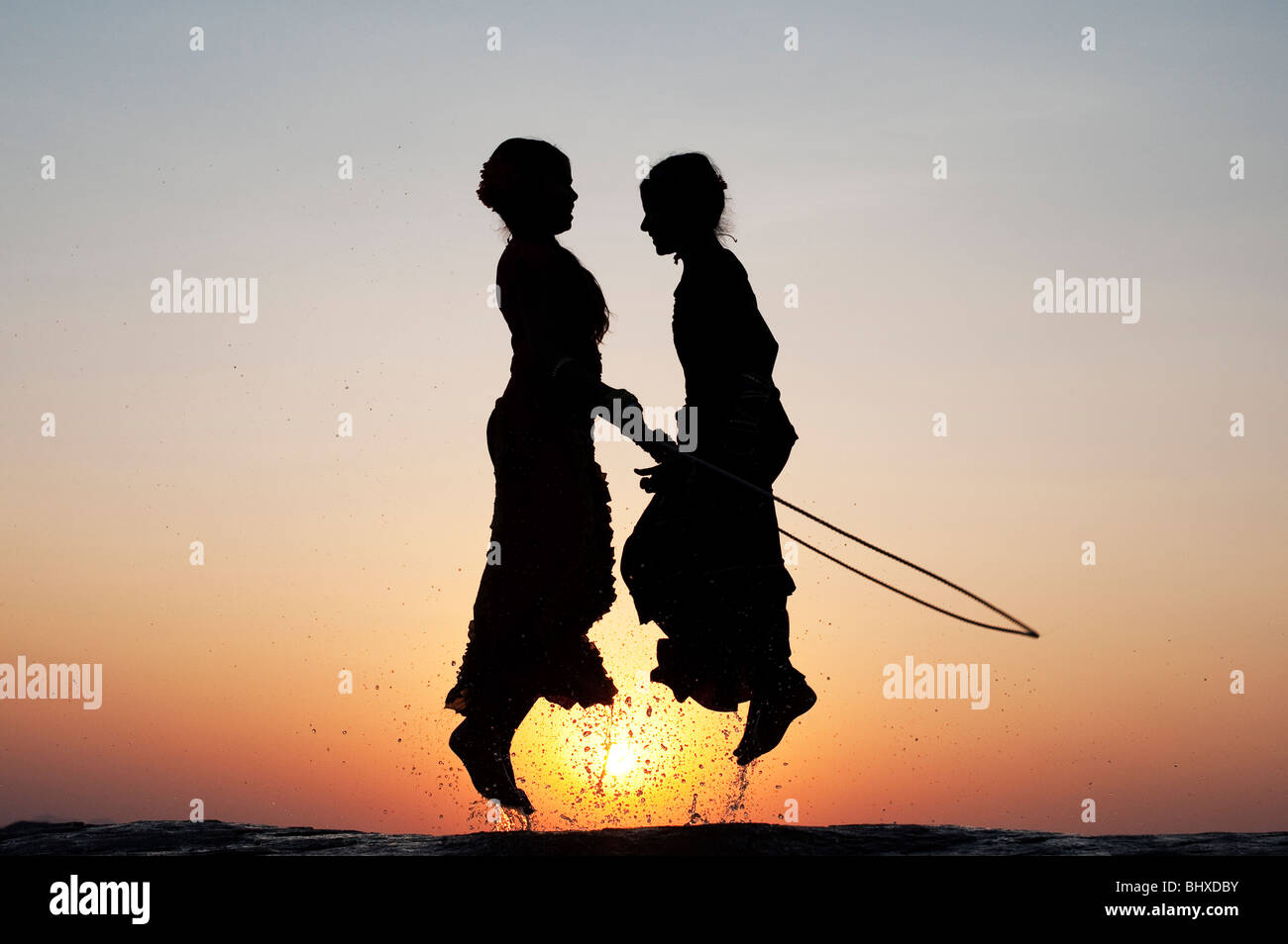 Silhouette of young Indian girls skipping in water at sunset. India ...