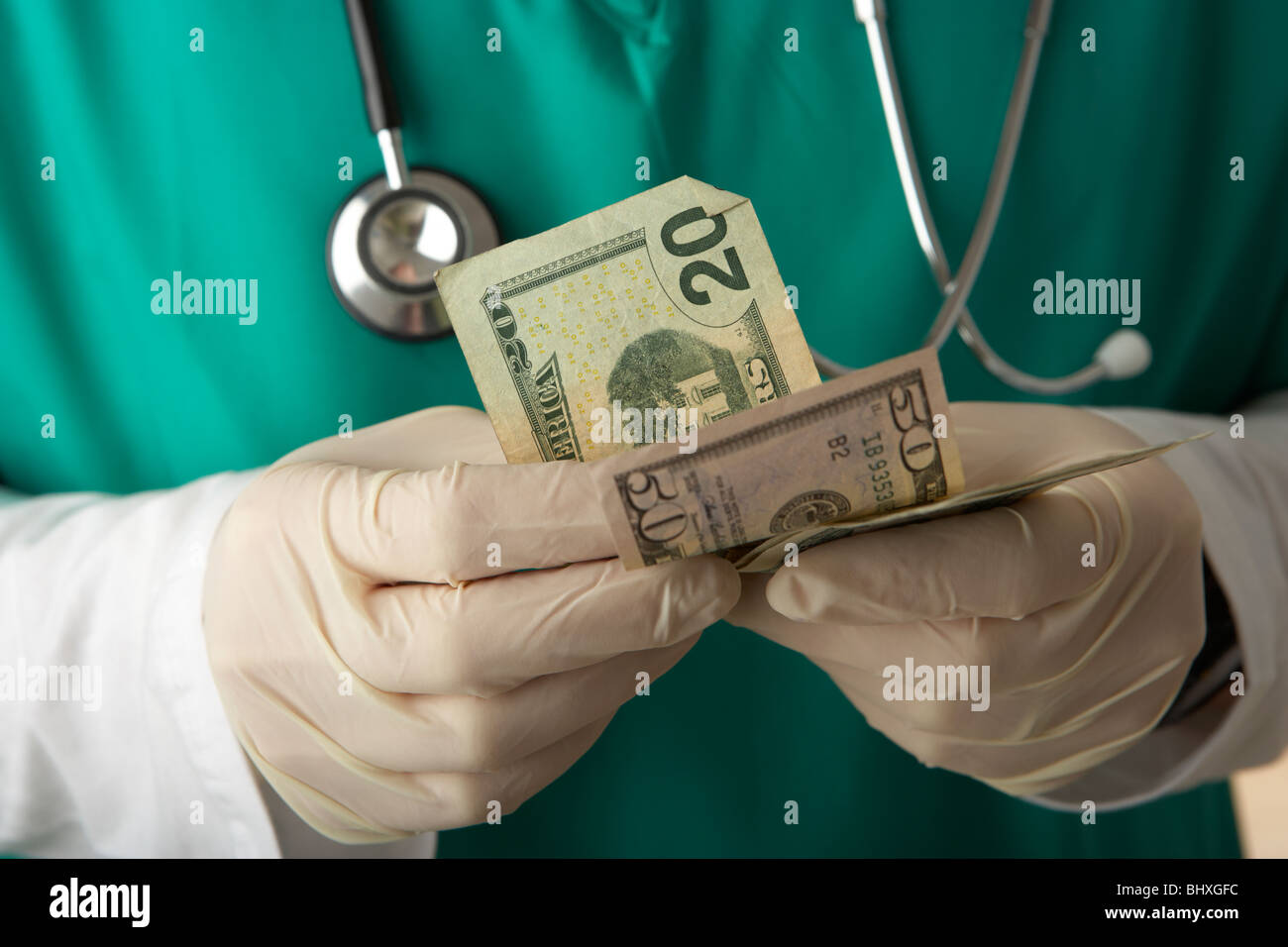man wearing medical scrubs and stethoscope counting us dollar banknotes ...
