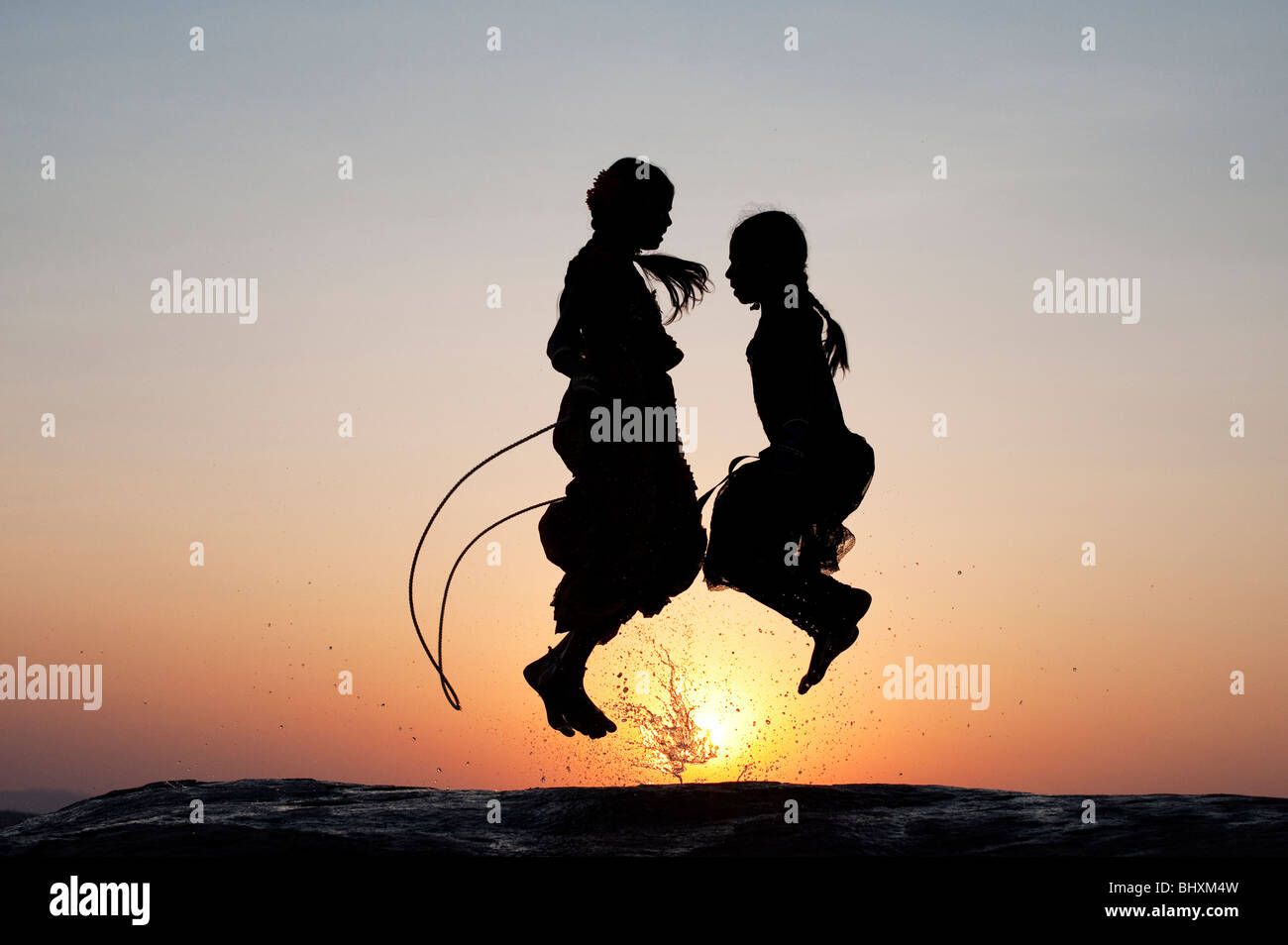 Silhouette of young Indian girls skipping in water at sunset. India ...