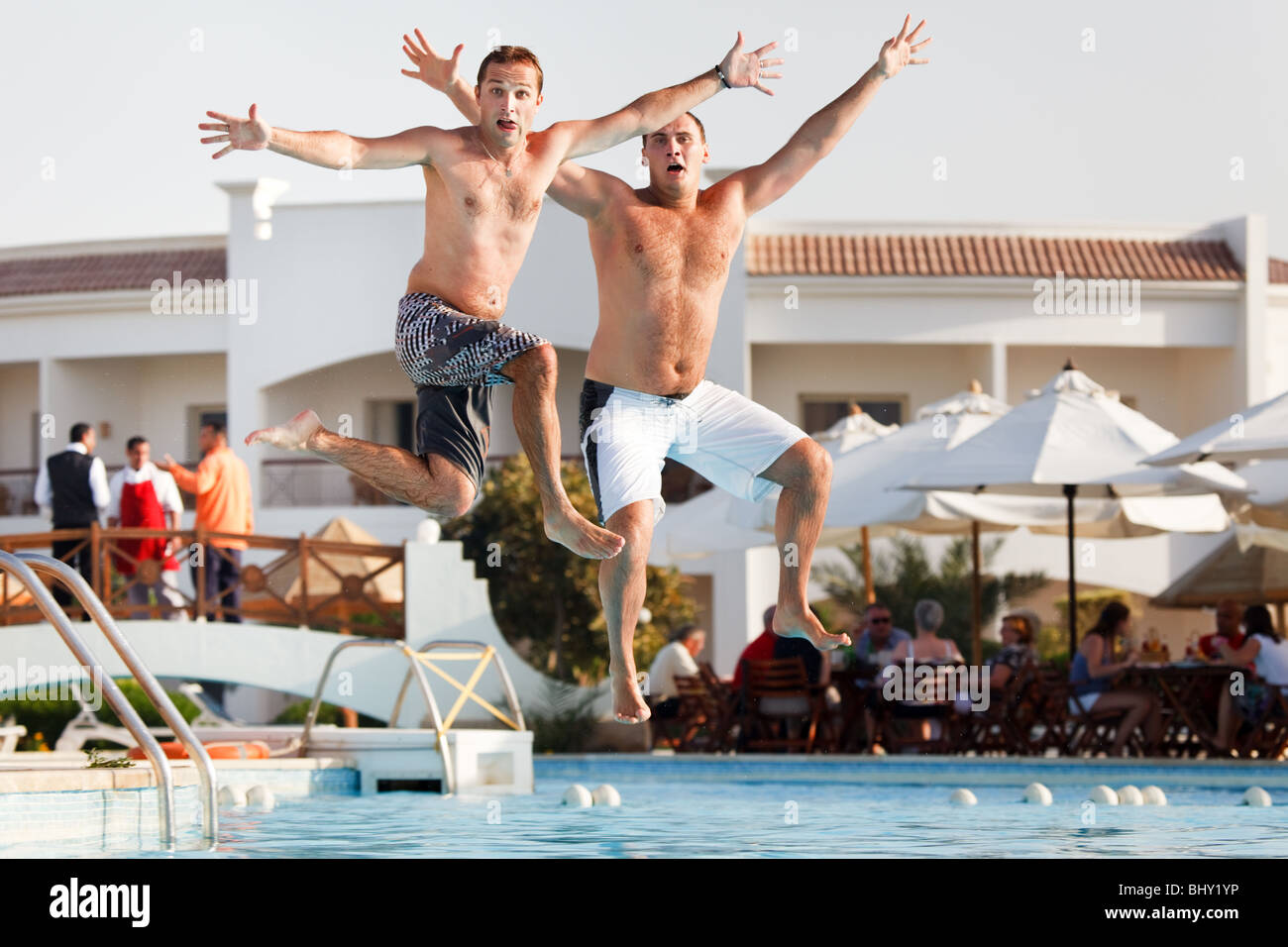 Two men jumping in swimming pool. Low angle view from the swimming pool ...