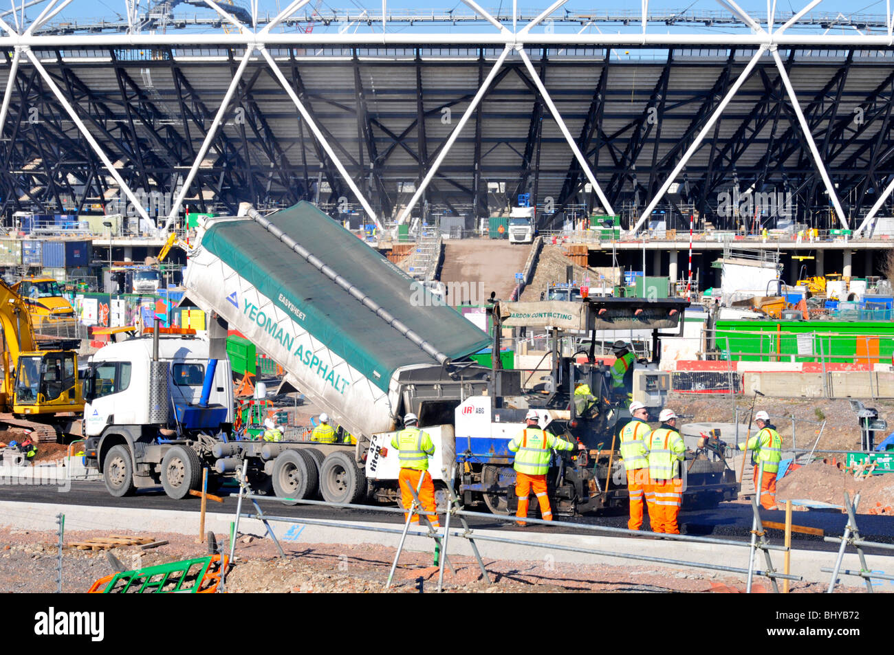 Close up of tipper lorry truck tipping tarmac into road laying machine ...