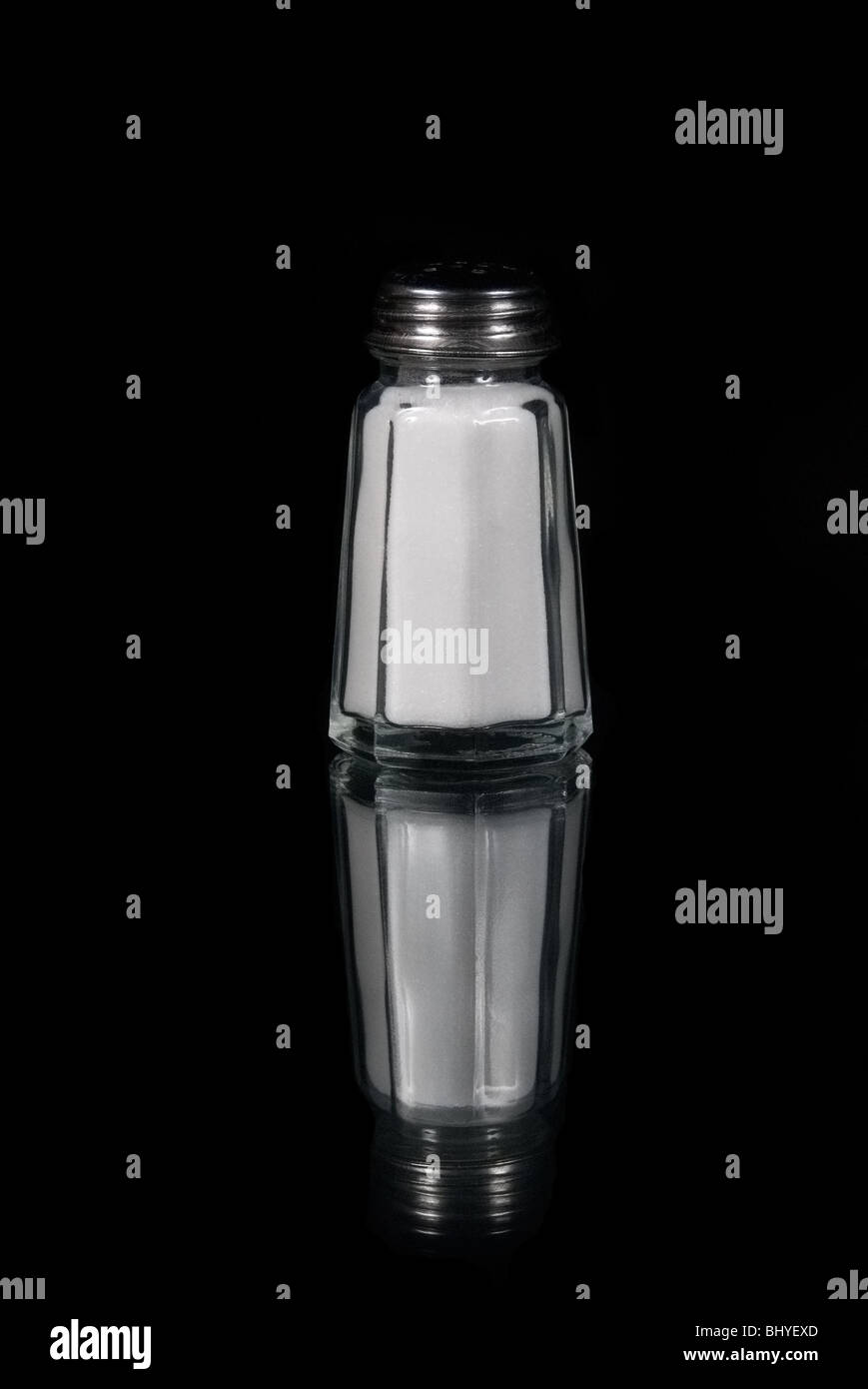 A glass Salt Shaker or dispenser on a reflective black background Stock ...