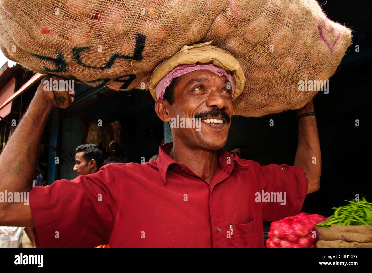 A porter carrying a large bag of shallots on his head. Kollam, Kerala ...