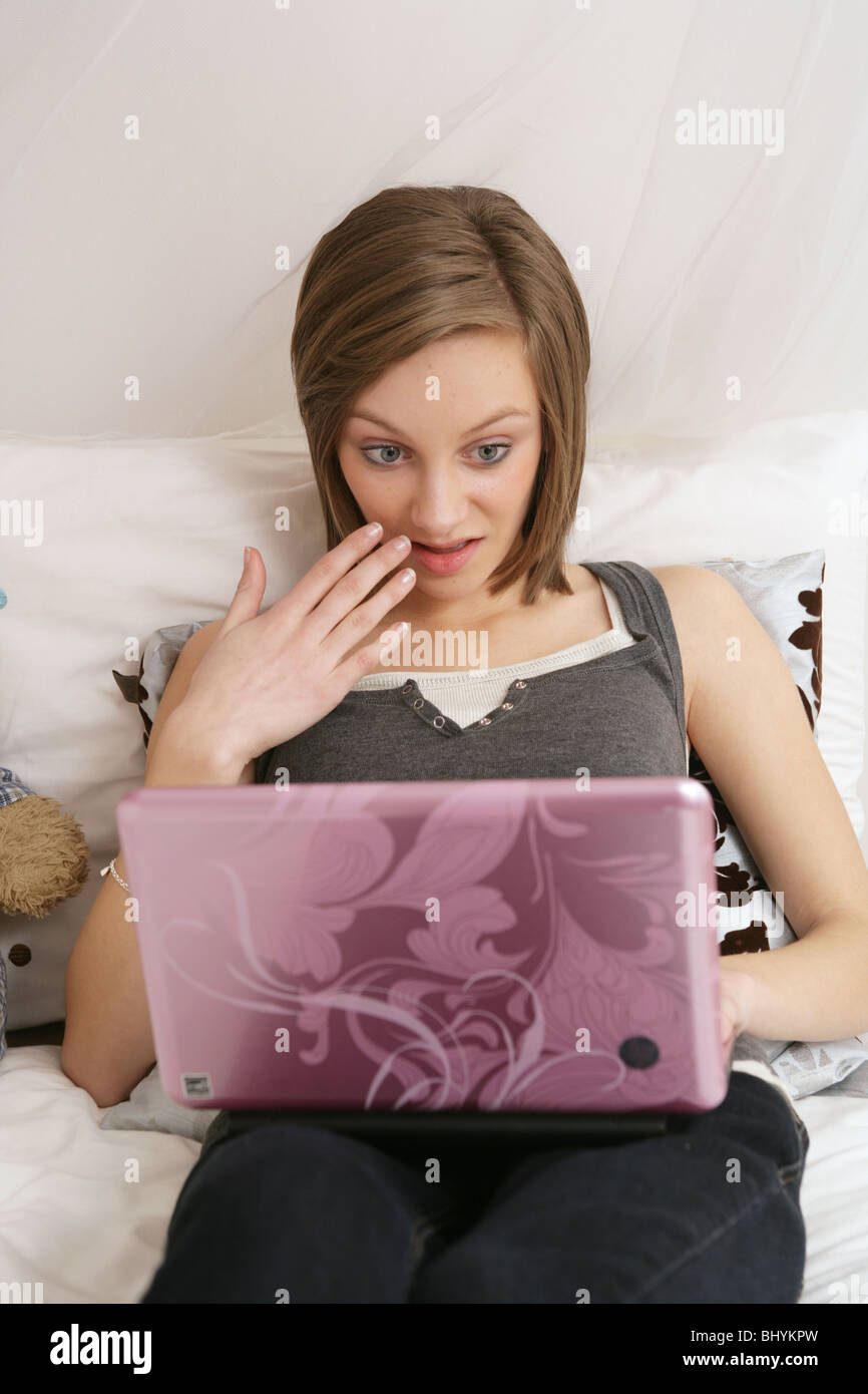 Pretty 14 year old girl lying on her bed using a net book and looking ...